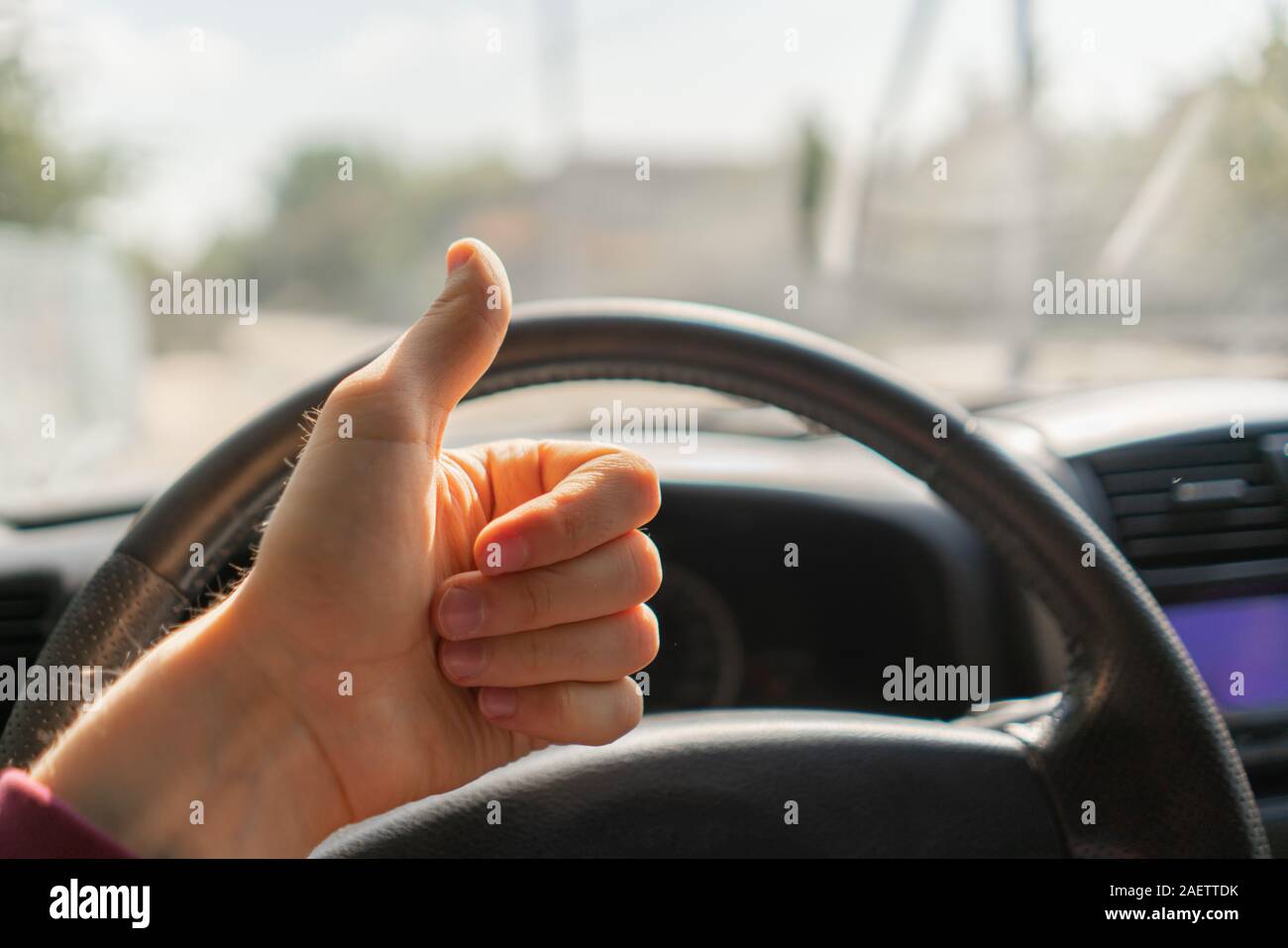 a first person view of driver showing thumb up in front of steering ...