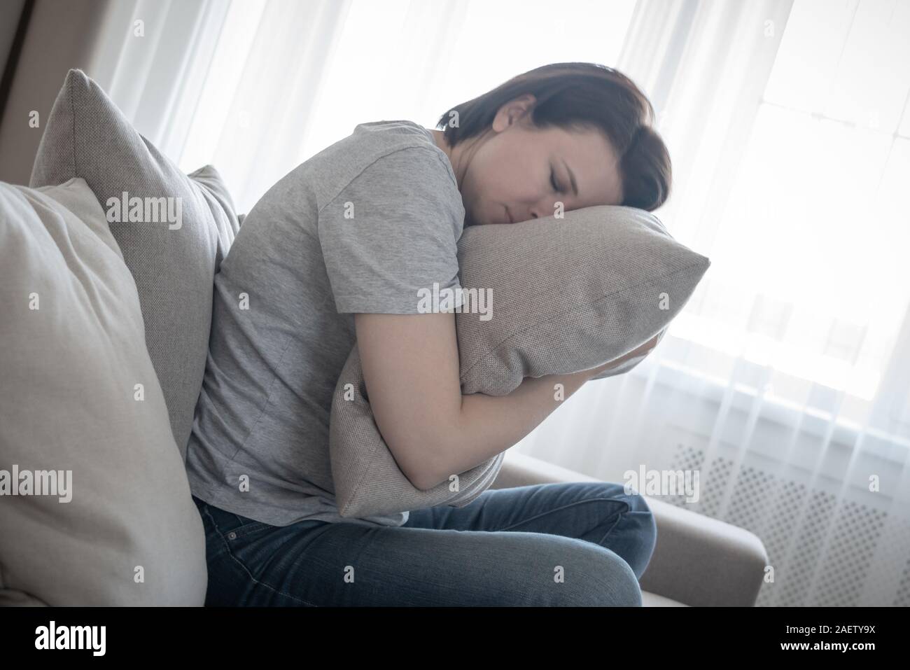 Sad depressed woman at home, she is sitting on the couch and hugging a ...