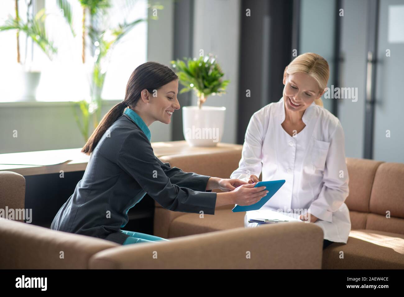 Dark-haired young female intern showing something on tablet to her ...