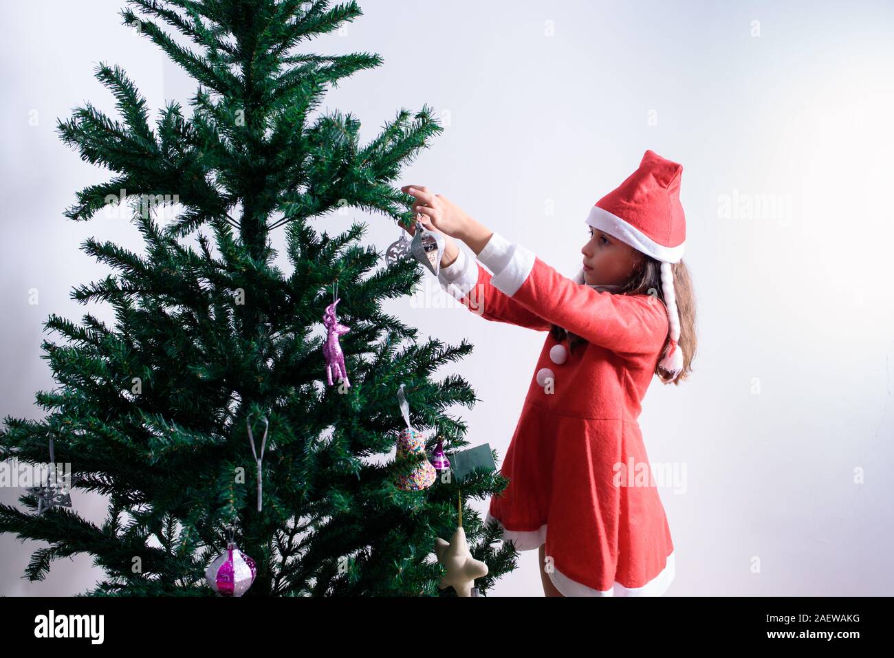 Little girl decorating Christmas tree. Disguised as Santa Claus. On ...