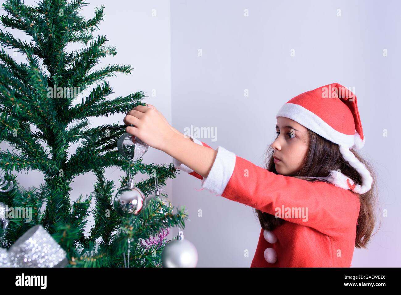 Little girl decorating Christmas tree. Disguised as Santa Claus. On ...