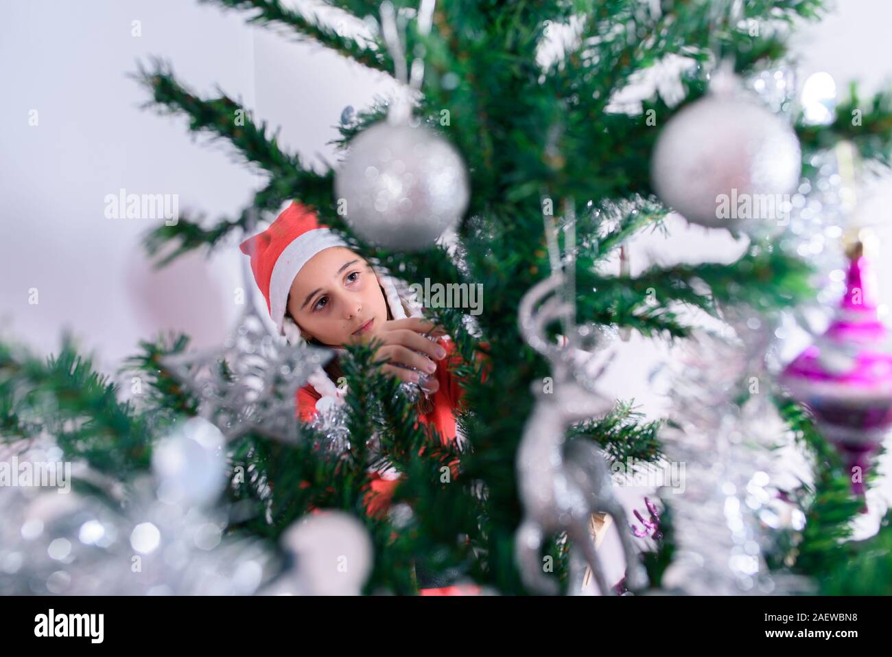 Little girl decorating Christmas tree. Disguised as Santa Claus. On ...