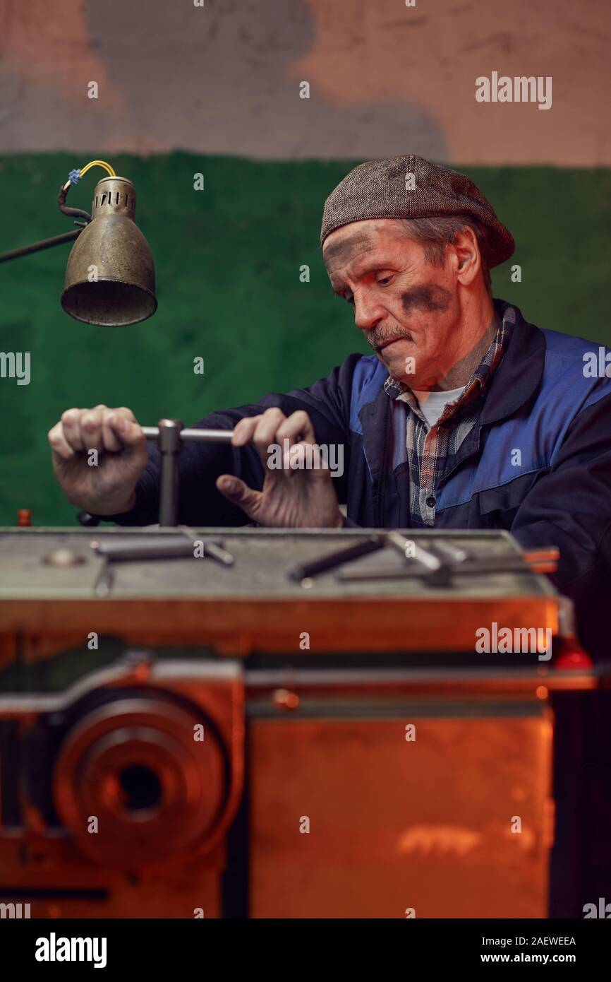 Serious senior man in work wear turning the lever while working at the ...