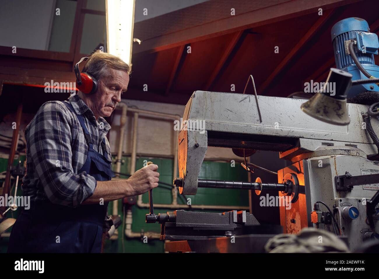 Serious senior operator wearing headphones standing at the lathe and ...