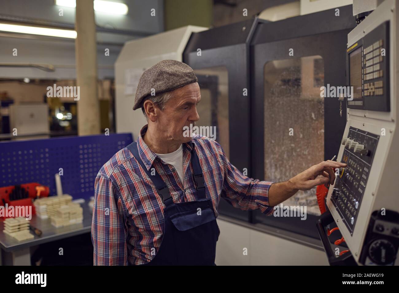 Senior operator in overalls standing in the factory and regulating the ...