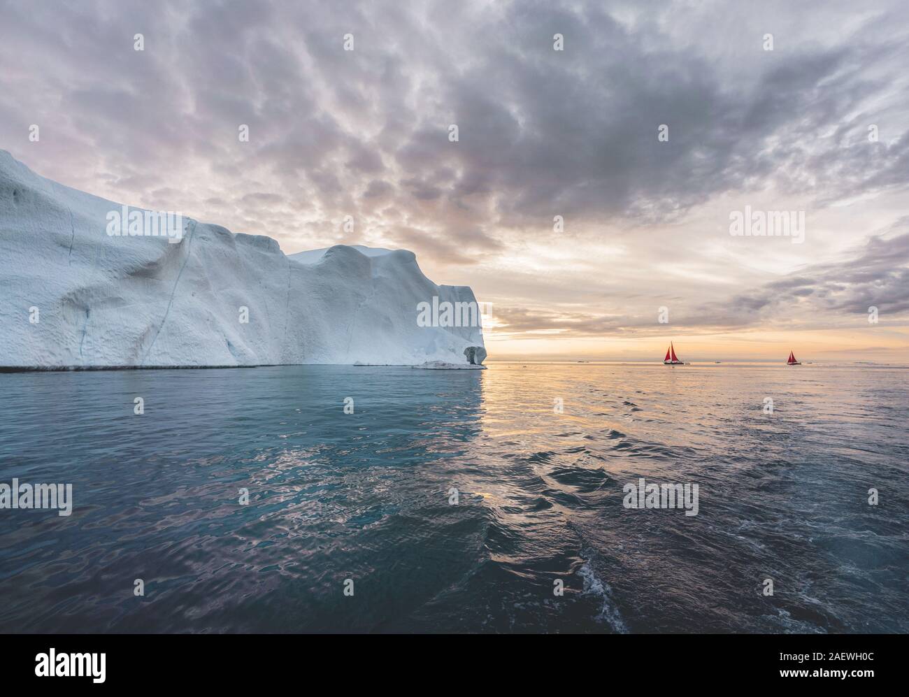 Beautiful red sailboat in the arctic next to a massive iceberg showing ...
