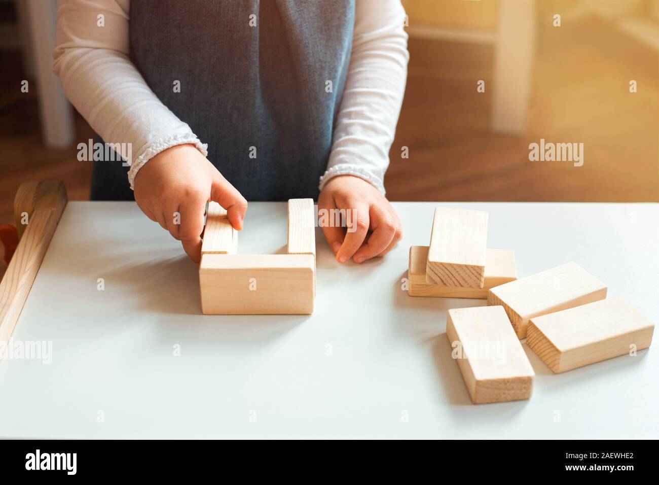 Little girl playing with wooden bricks at home. She builds little house ...