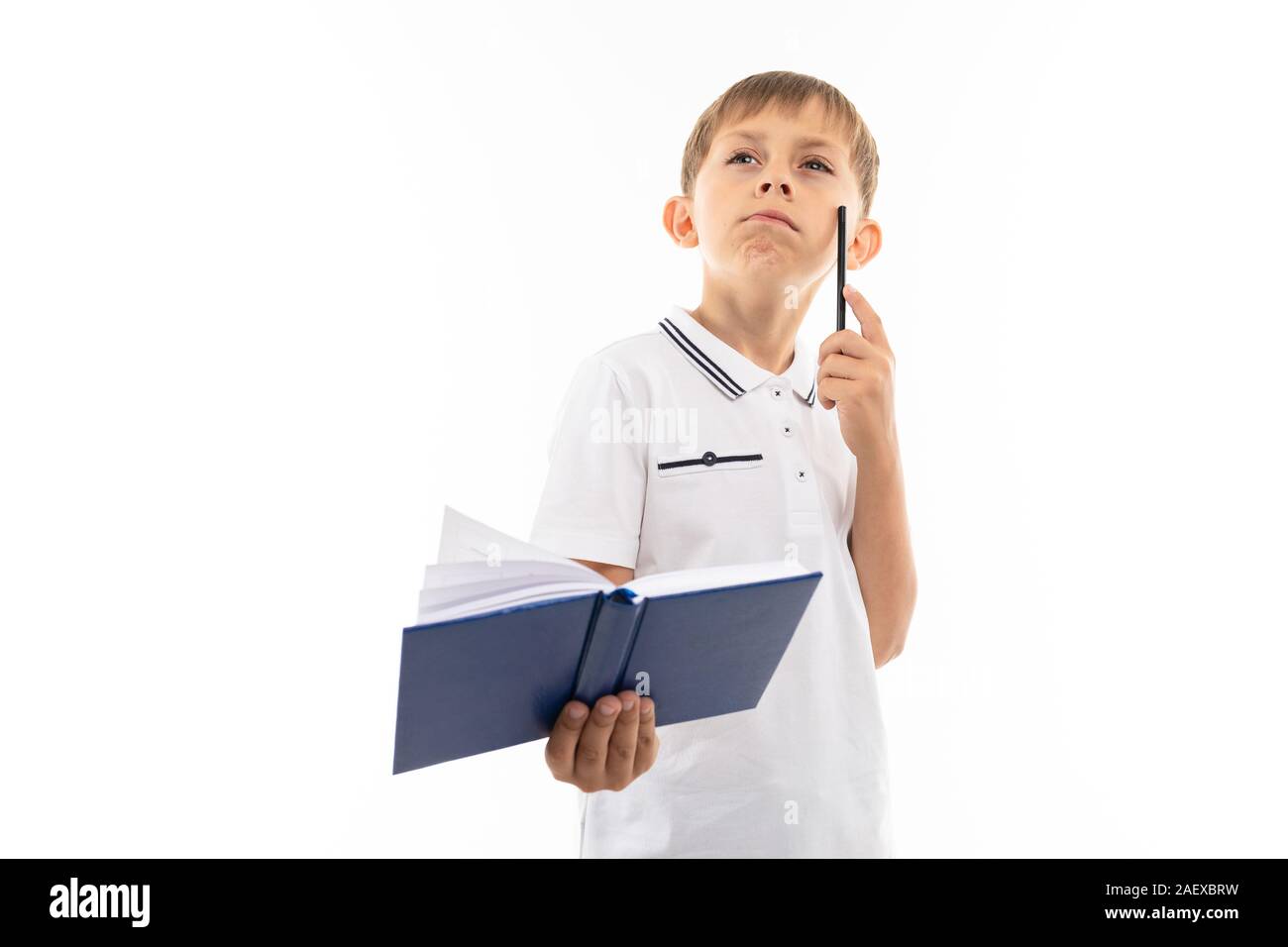 European boy thinks with a book and pen in his hands on a white ...