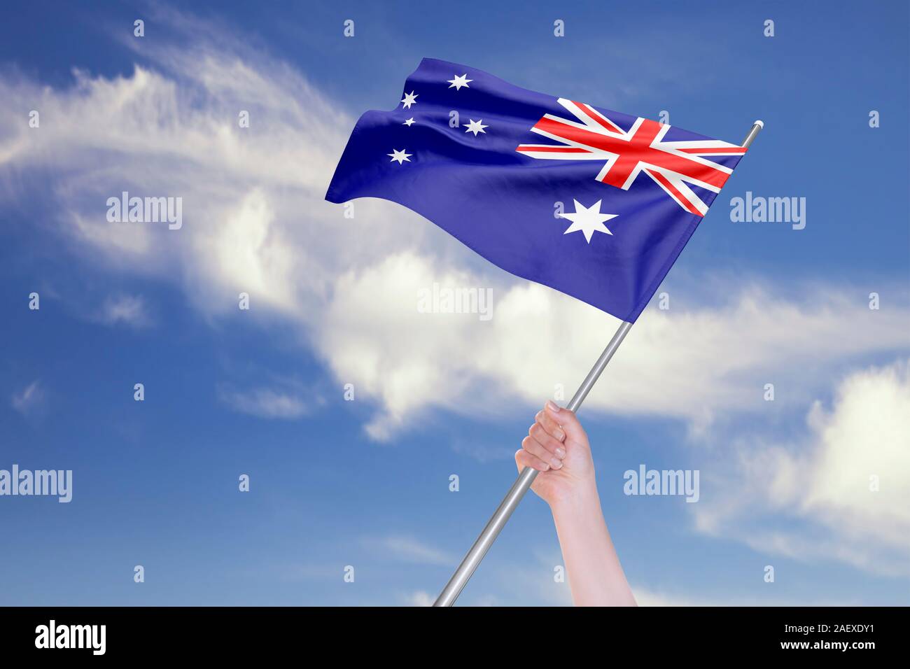 Female hand is waving Australian Flag against blue sky with clouds ...