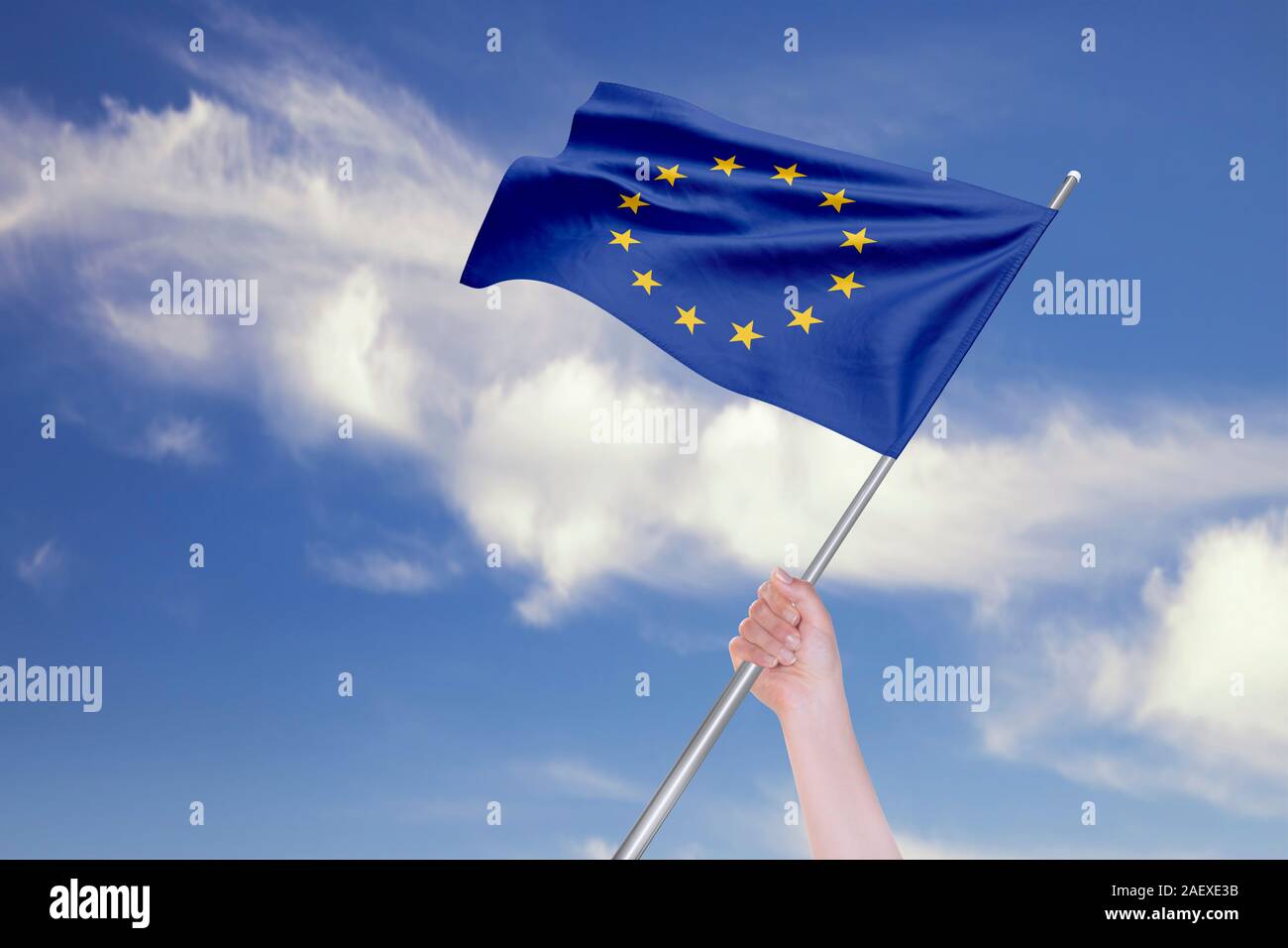 Female hand is waving European Union Flag against blue sky with clouds ...
