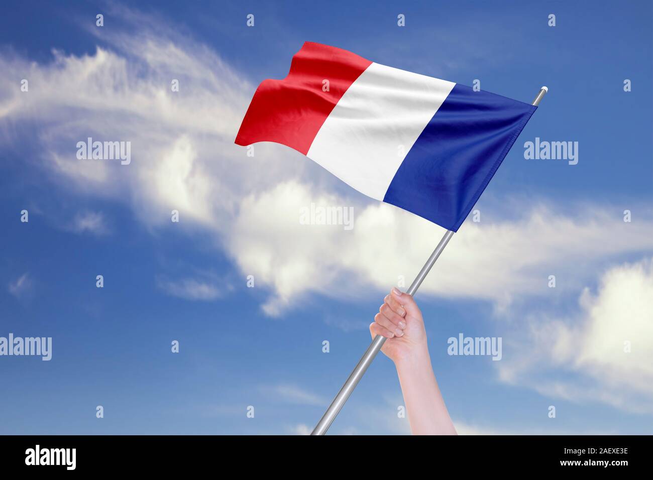 Female hand is waving French Flag against blue sky with clouds ...
