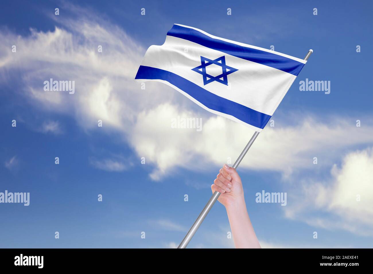 Female hand is waving Israeli Flag against blue sky with clouds ...
