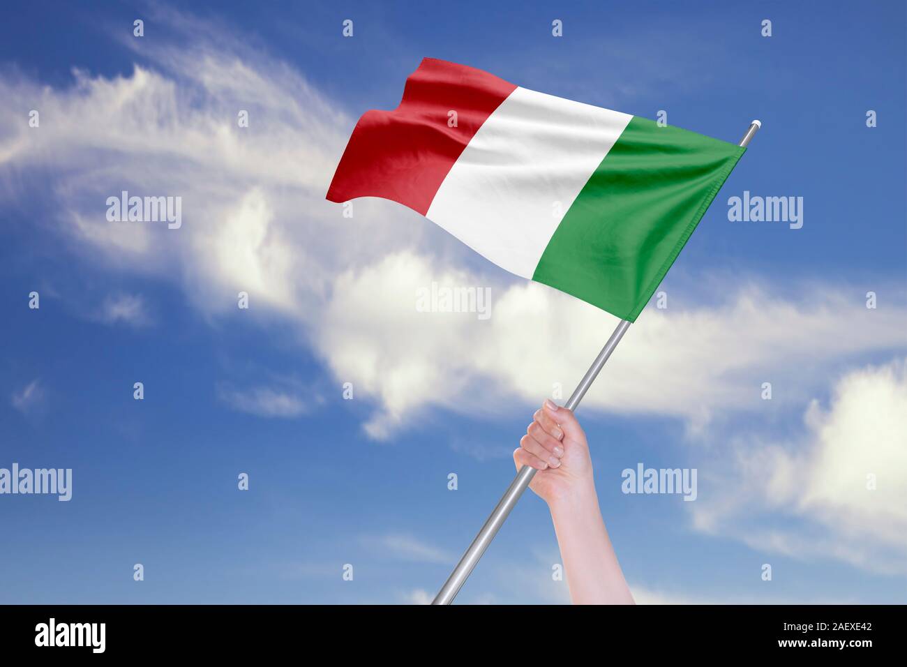 Female hand is waving Italian Flag against blue sky with clouds ...