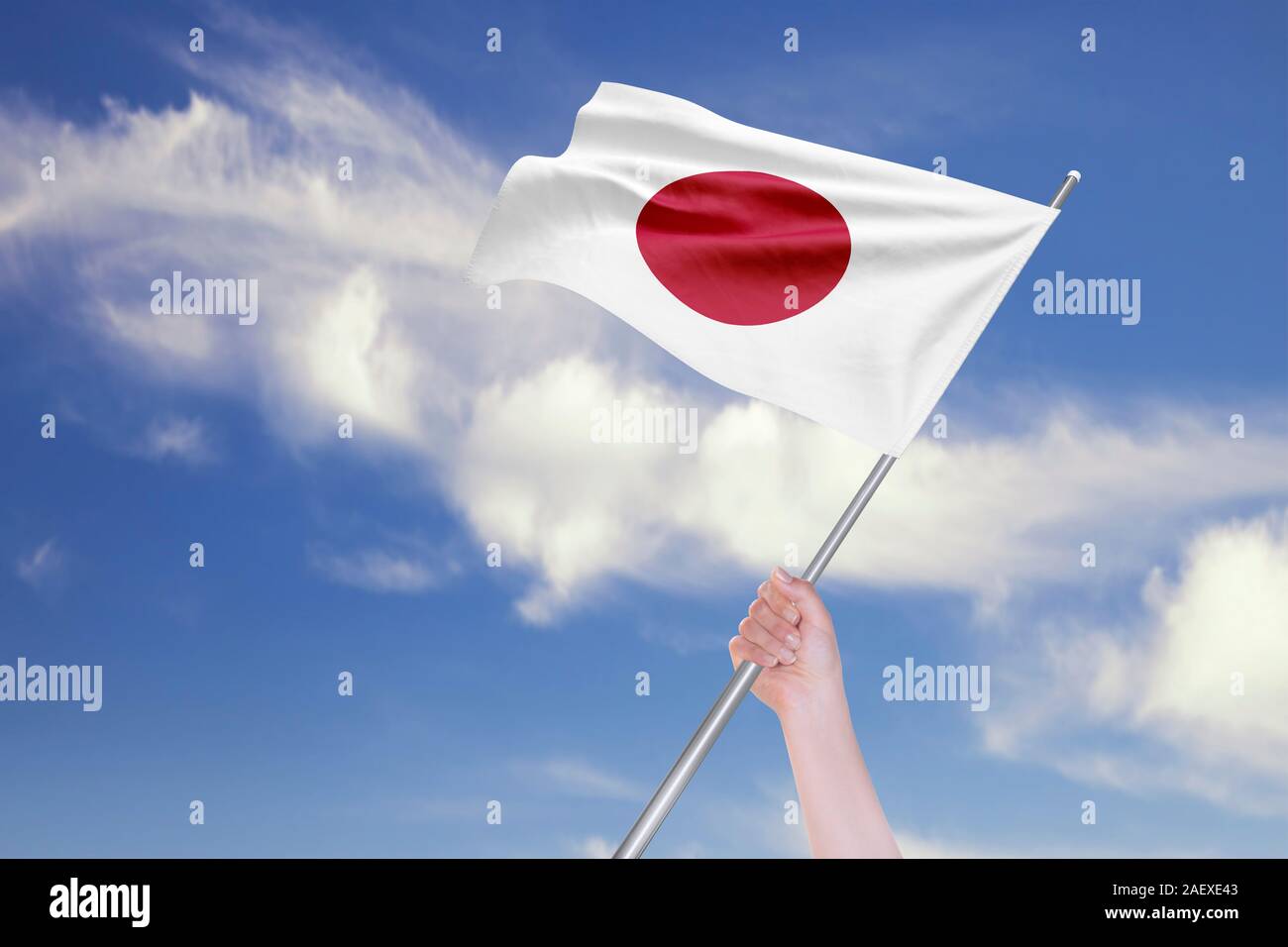 Female hand is waving Japanese Flag against blue sky with clouds ...