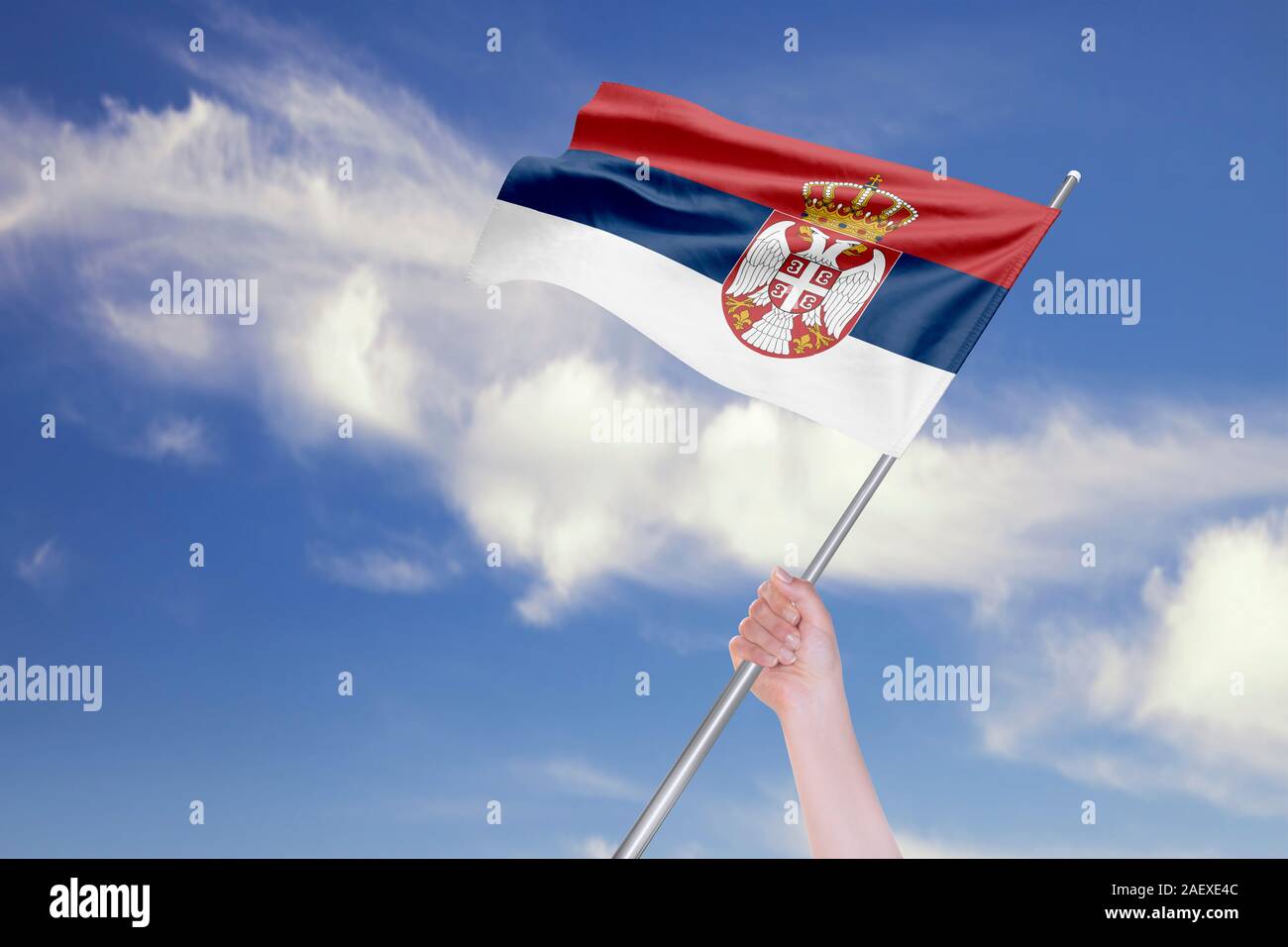 Female hand is waving Serbian Flag against blue sky with clouds ...