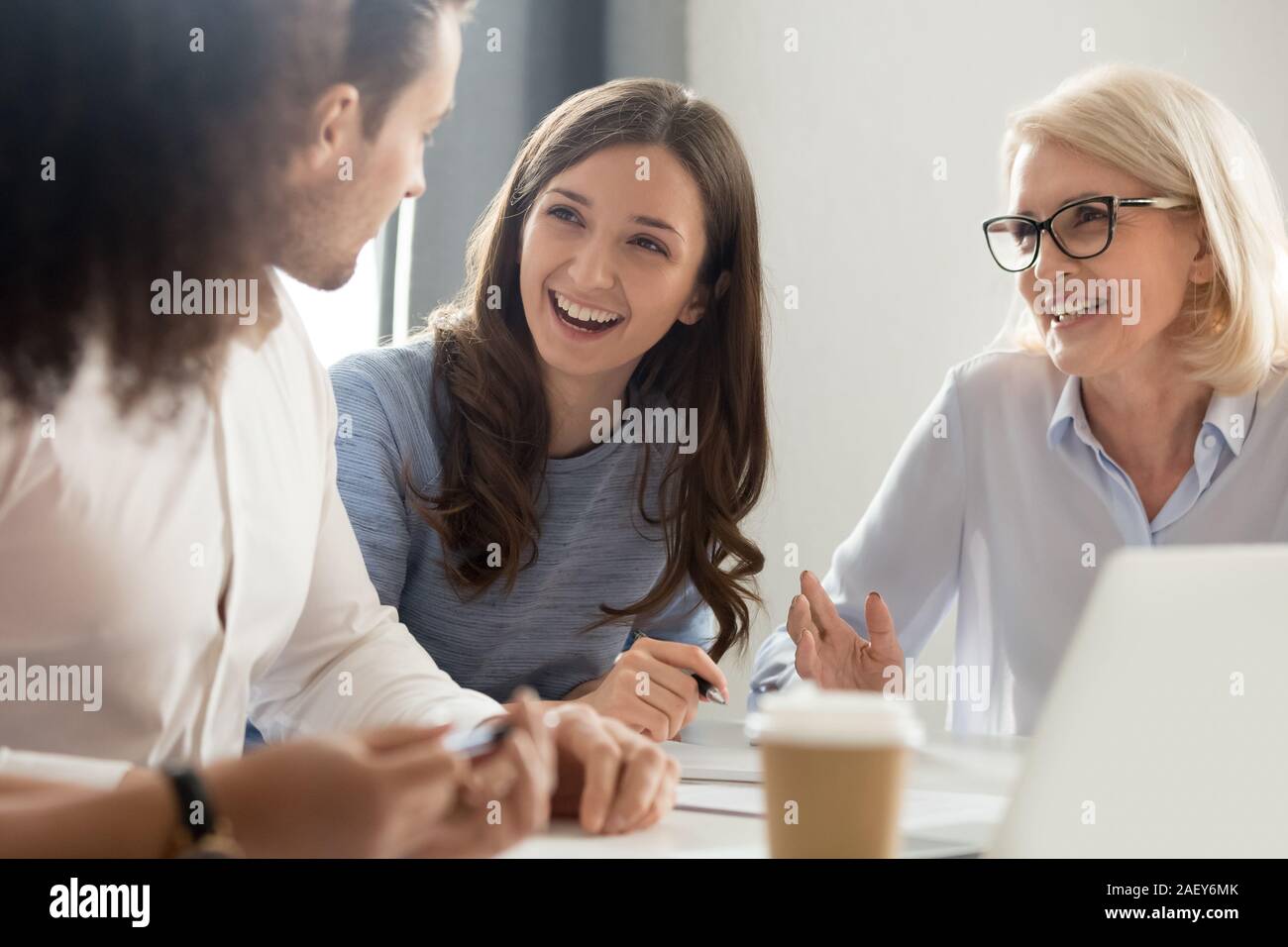 Diverse employees laugh talking sitting at desk in office Stock Photo ...