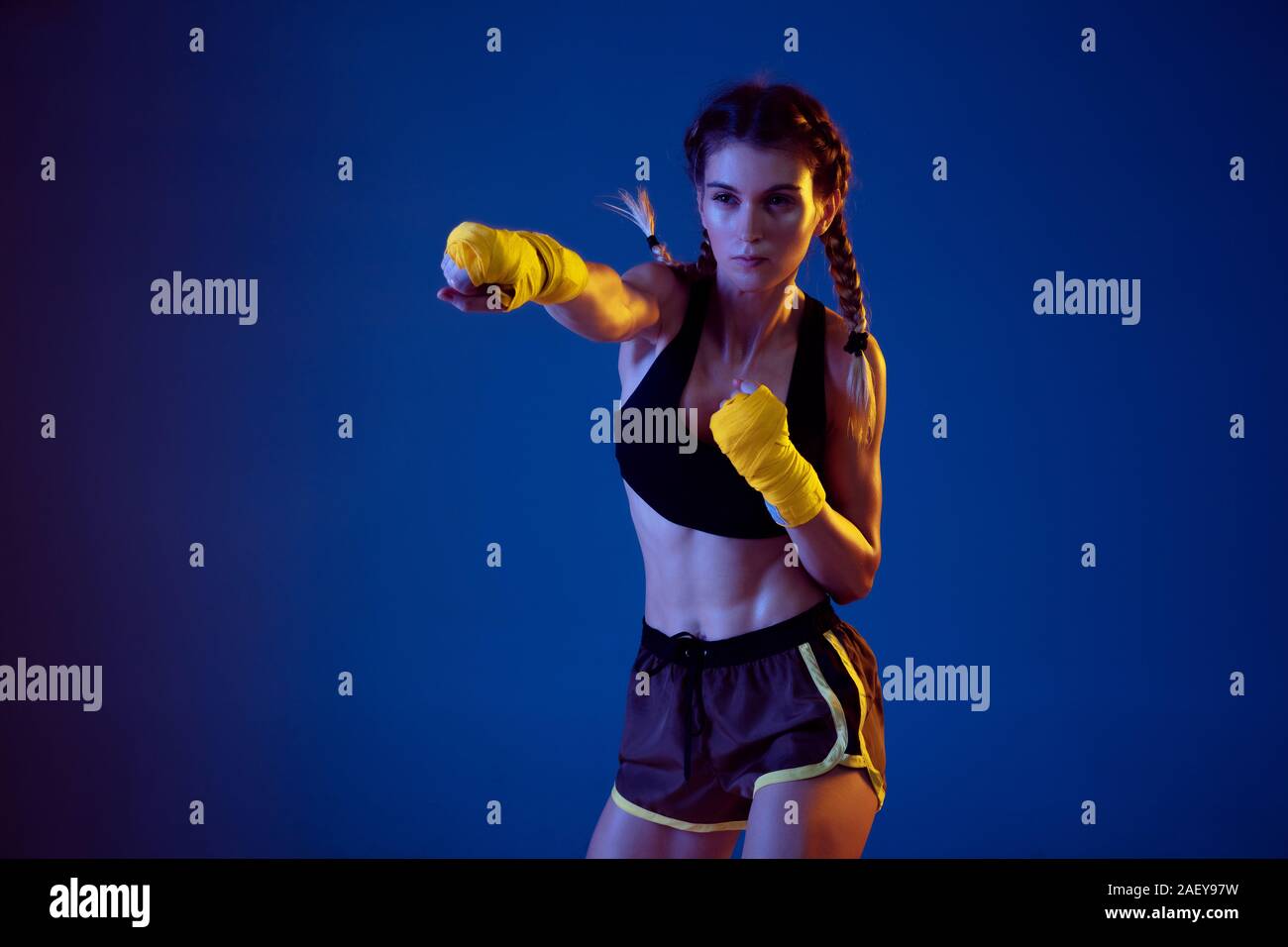 Sunshine. Fit caucasian woman in sportswear boxing on blue studio ...