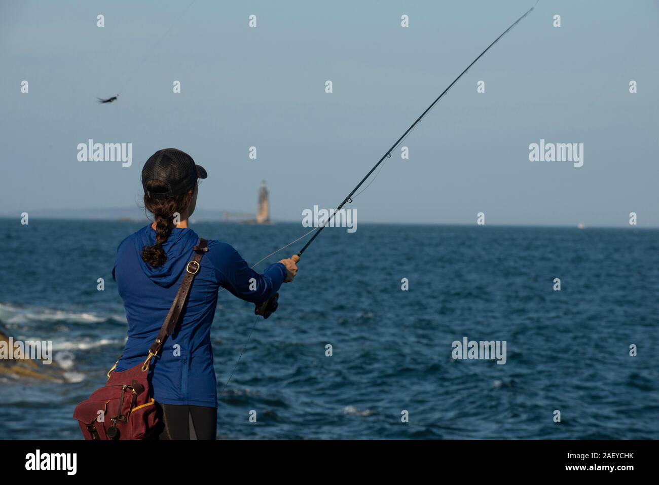 A woman in blue casting a fly rod near Portland HEadlight in Maine ...