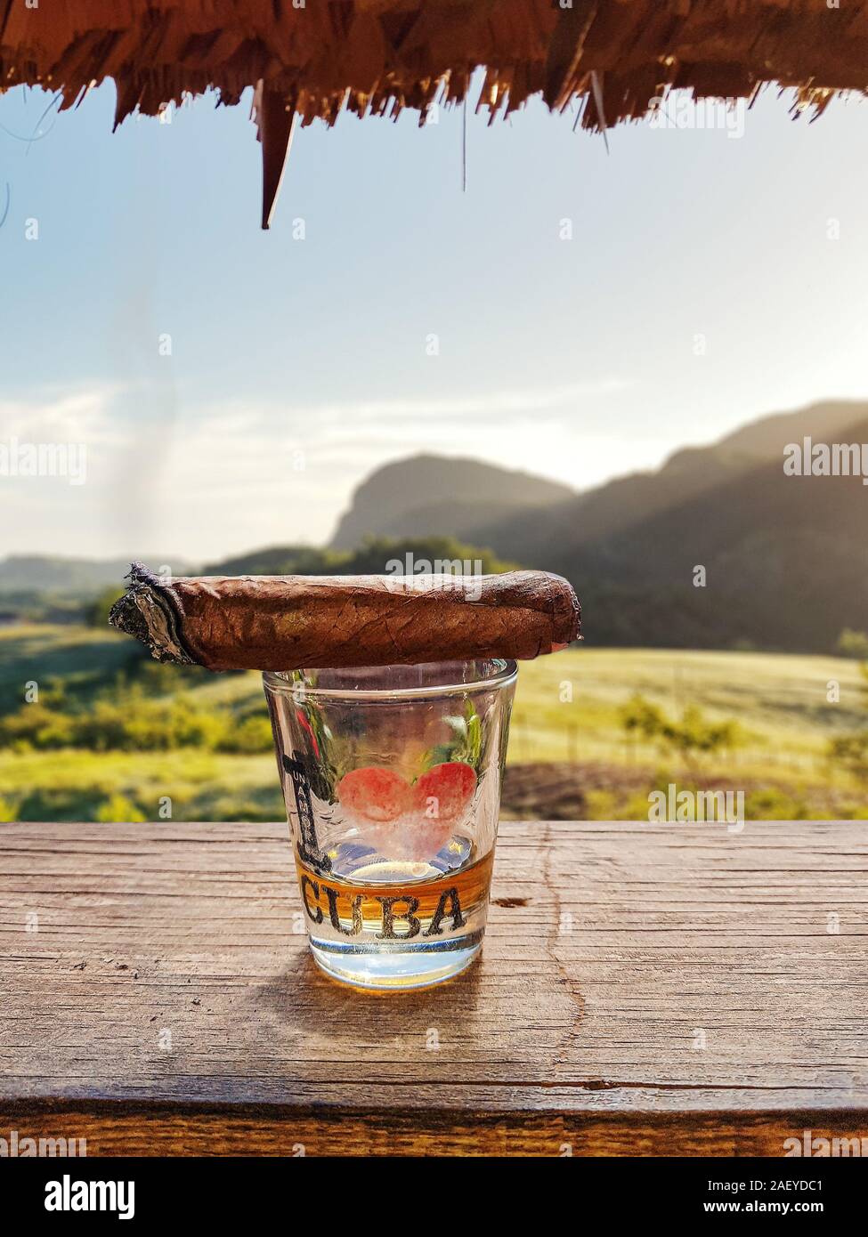 Glass of cuban rum with a smoking cigar lying on the rim of the glass ...