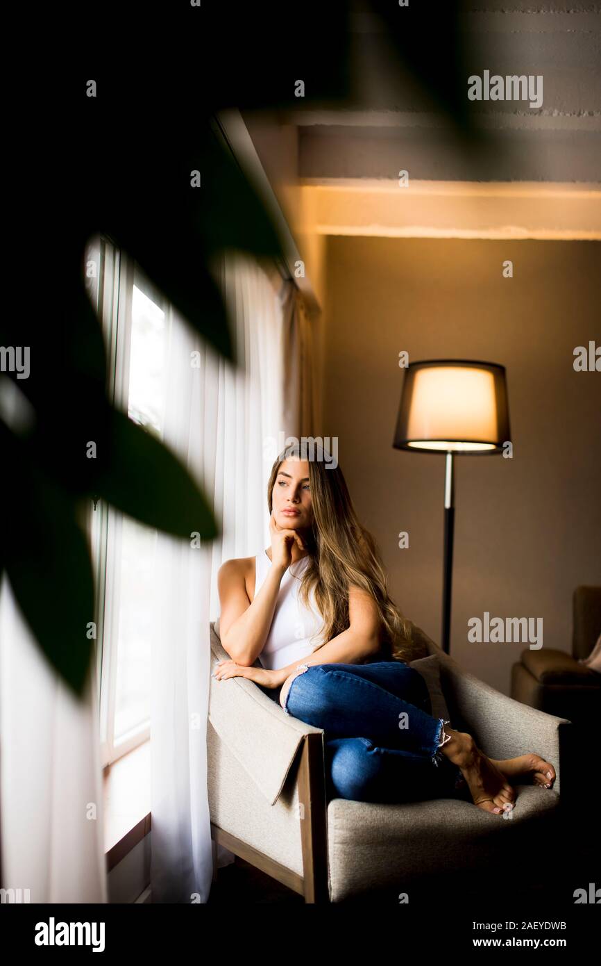 Beautiful young woman sitting by the window in apartment Stock Photo ...