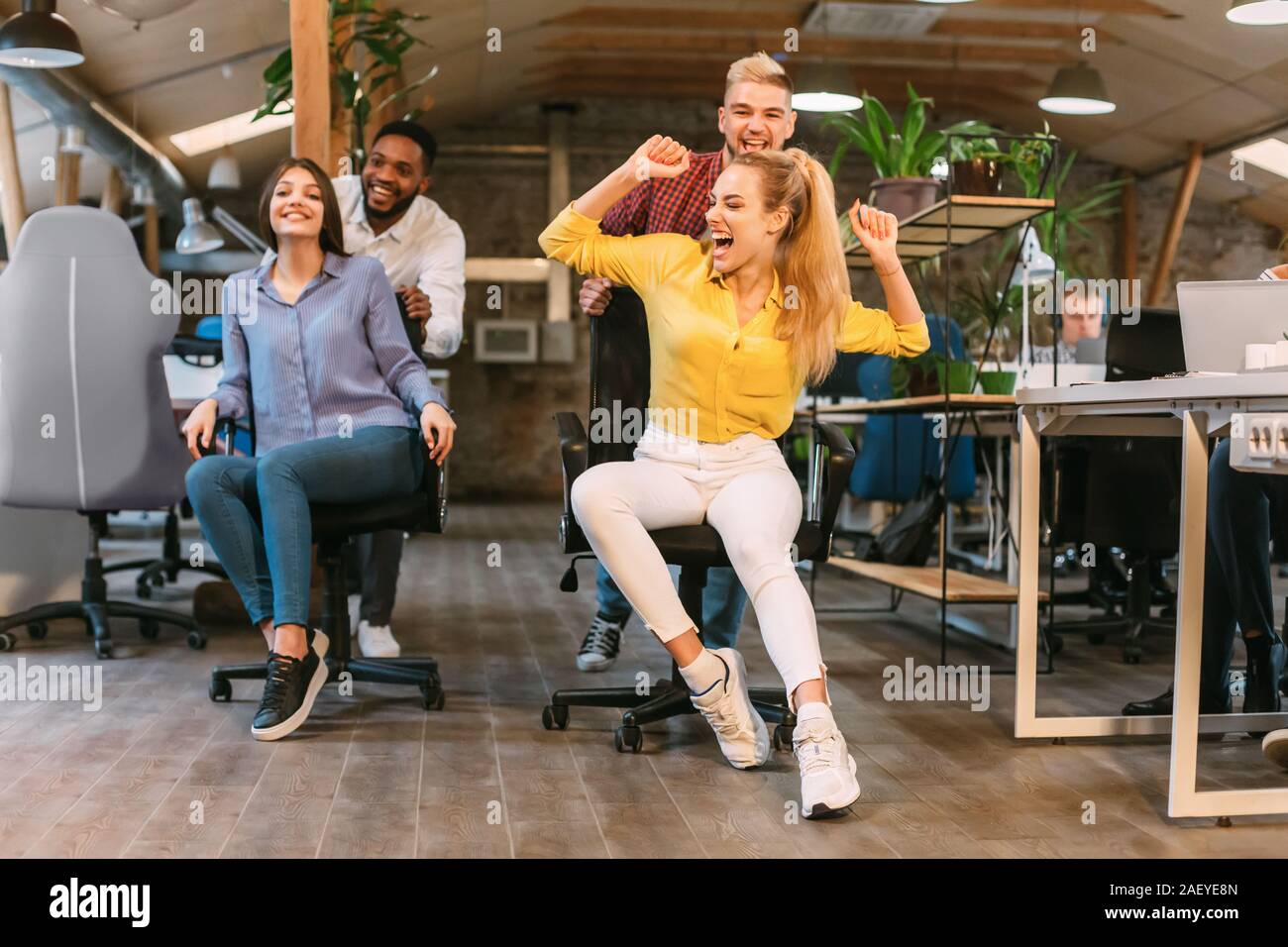 Positive colleagues having fun in office, enjoying office chair race ...