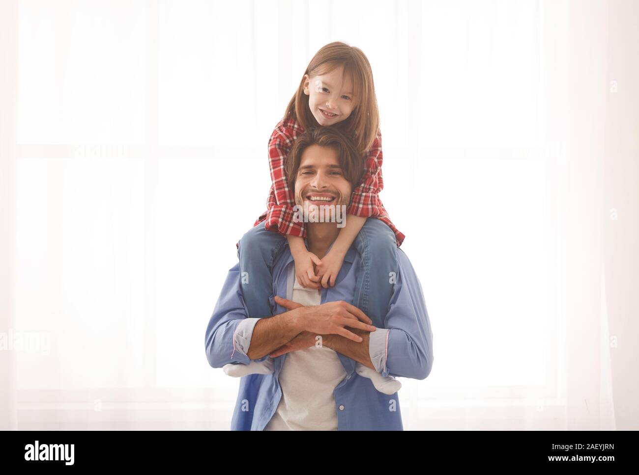 Smiling dad carrying his lovely cheerful little daughter on shoulders, having fun together at ...