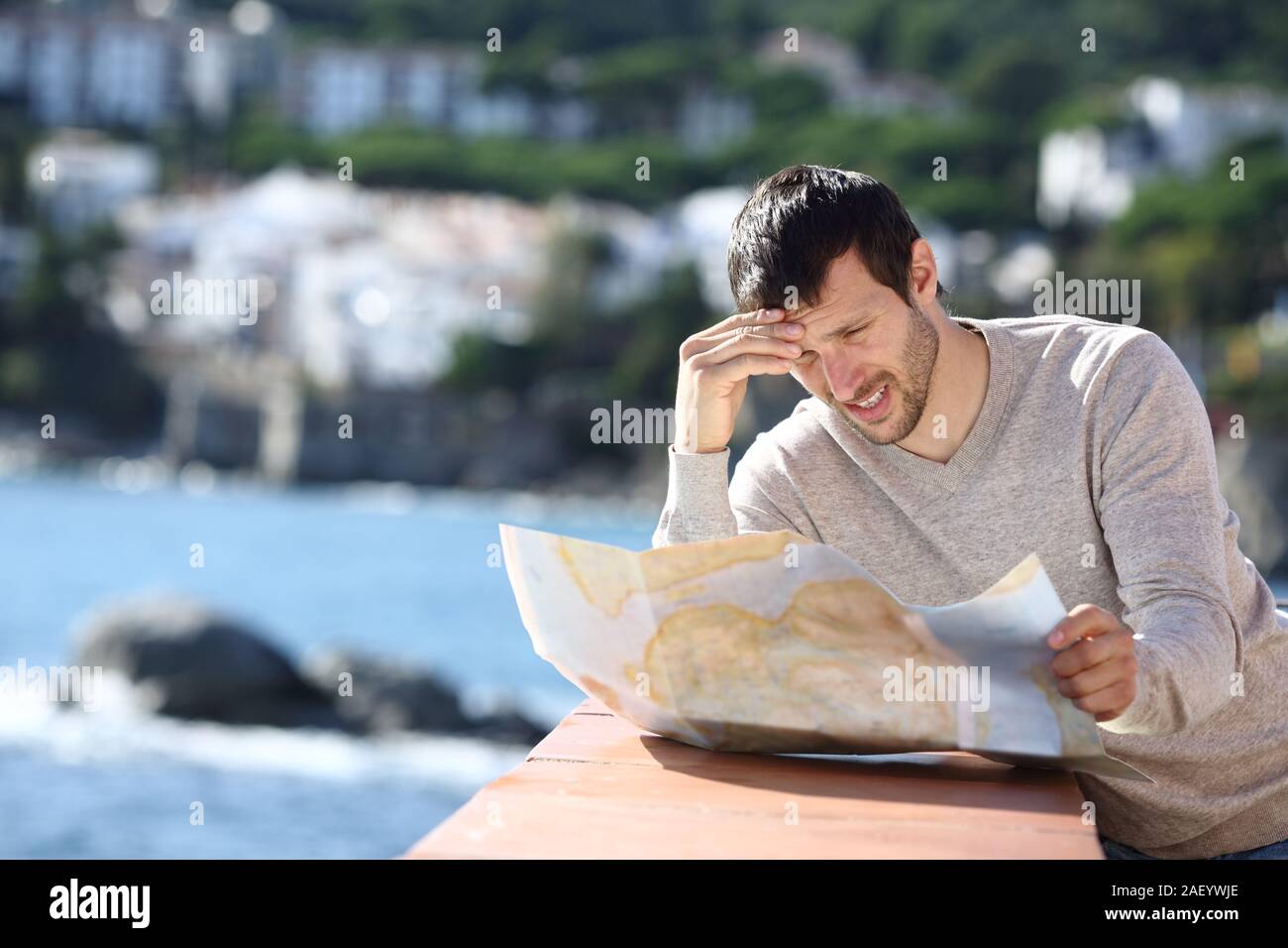 Worried lost tourist checking paper map on vacation in a coast town ...