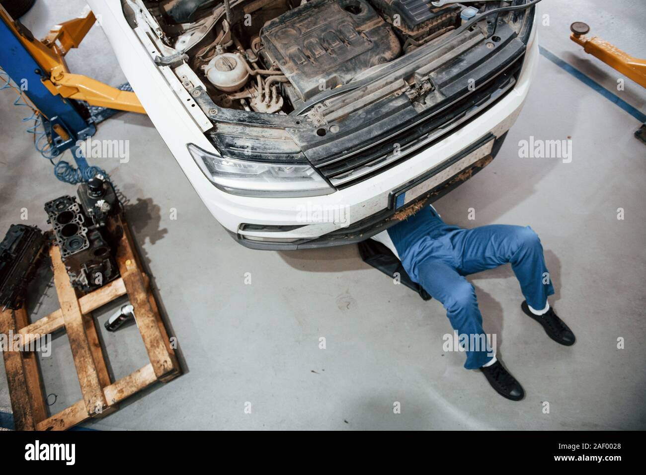 Under the car. Employee in the blue colored uniform works in the ...