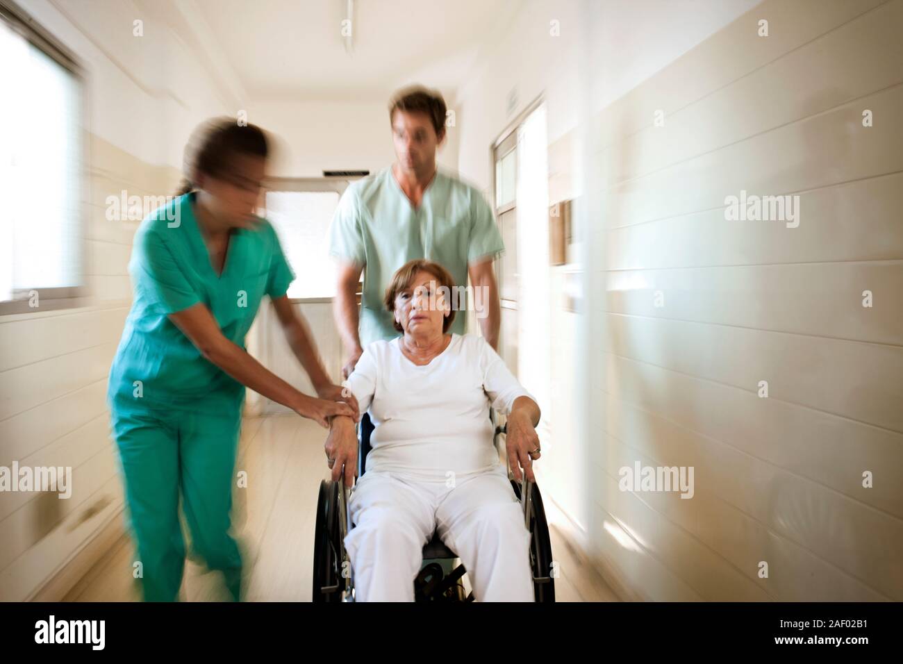 Doctor and nurse rushing a patient down a corridor in a wheelchair ...