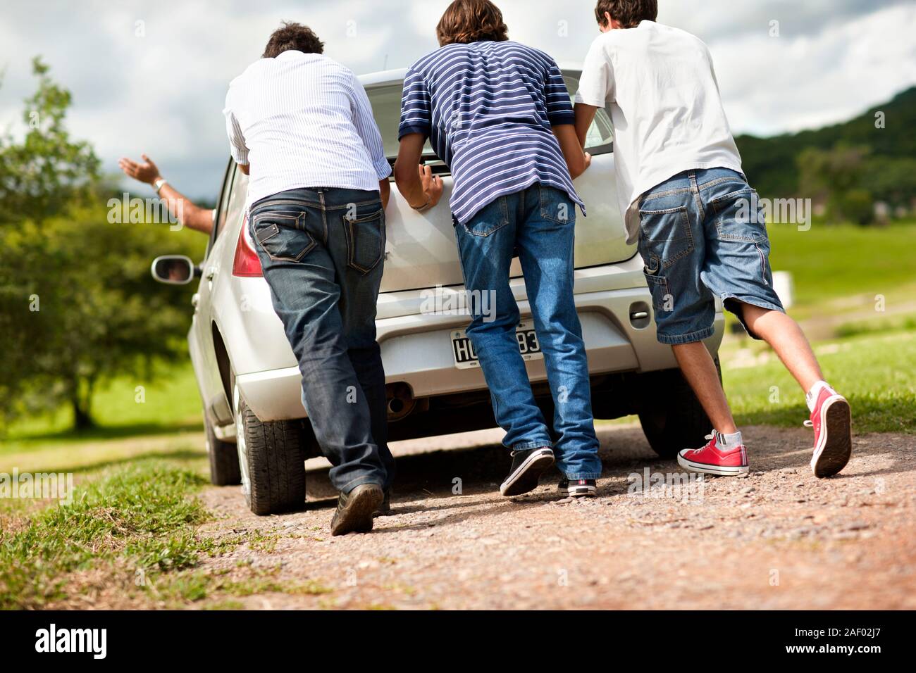 Three teenage boys pushing a broken down car in the country Stock Photo ...