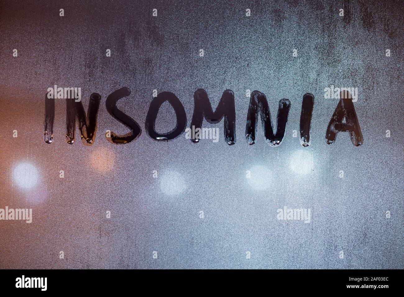the word insomnia written on night wet window glass close-up with ...
