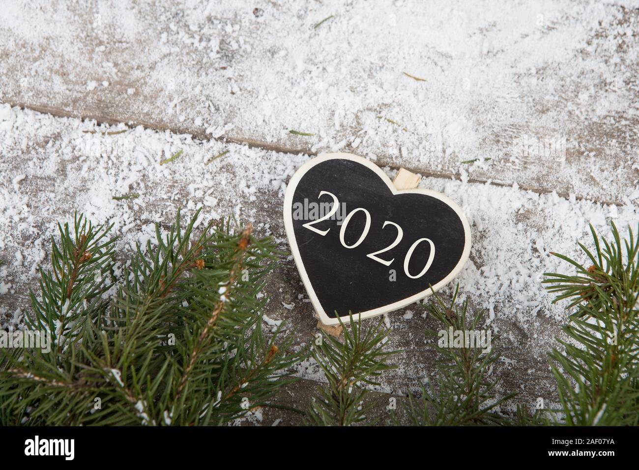 Blackboard in heart shape with text "2020", fir branches on a snow ...