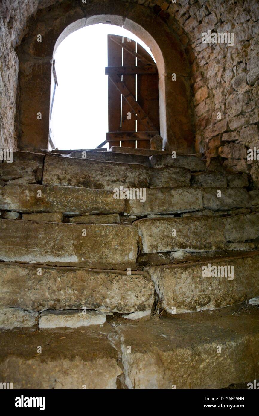 Old stone steps in a castle, looking up to an open door in the bright ...
