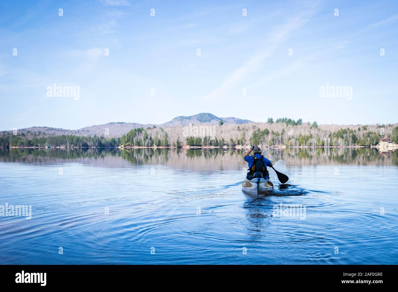 Man paddling canoe on calm water under blue sky Stock Photo - Alamy