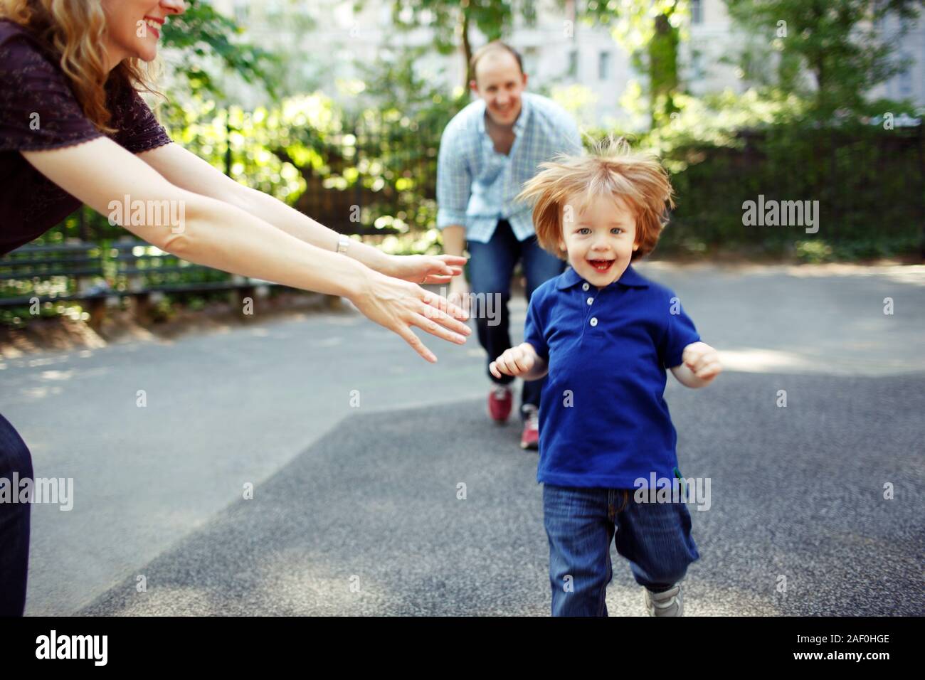 Boy running towards camera as parents playfully chase him Stock Photo ...