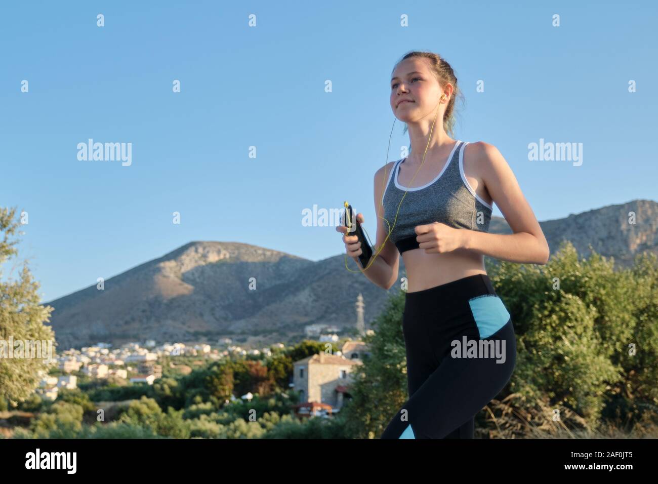 Running young teenager girl in fitness clothes headphones with ...