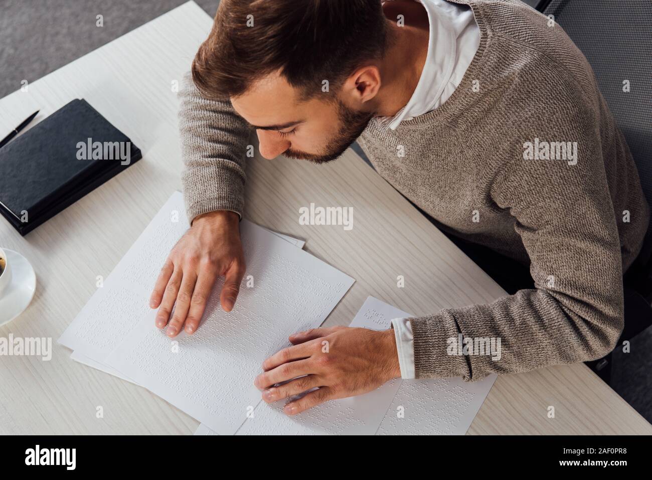 High angle view on visually impaired man reading braille font at table ...