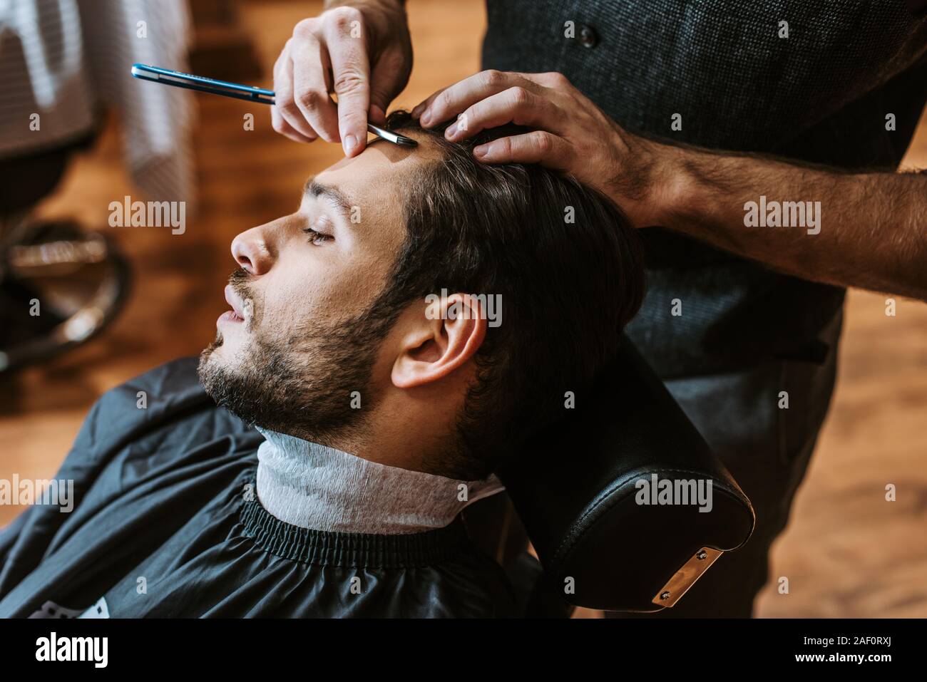 barber holding sharp razor while doing haircut to handsome man Stock ...