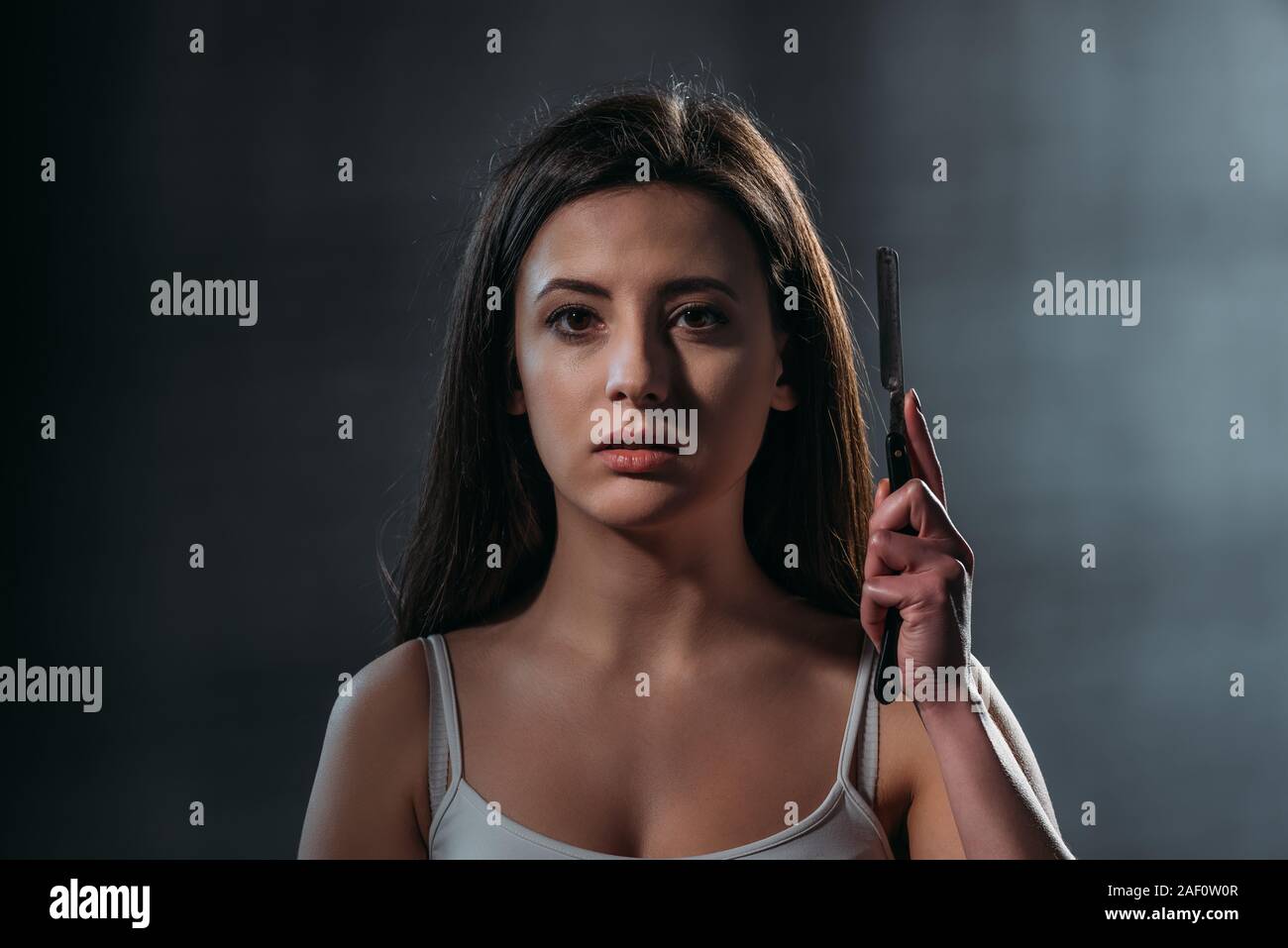 depressed young woman looking at camera while holding straight razor on ...