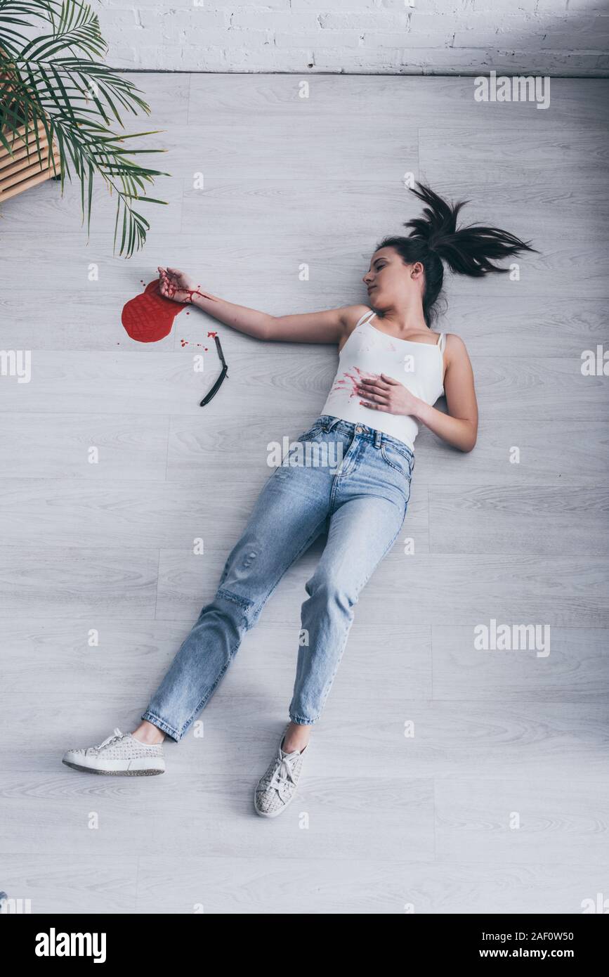 top view of unconscious woman with cut bleeding veins lying on floor ...