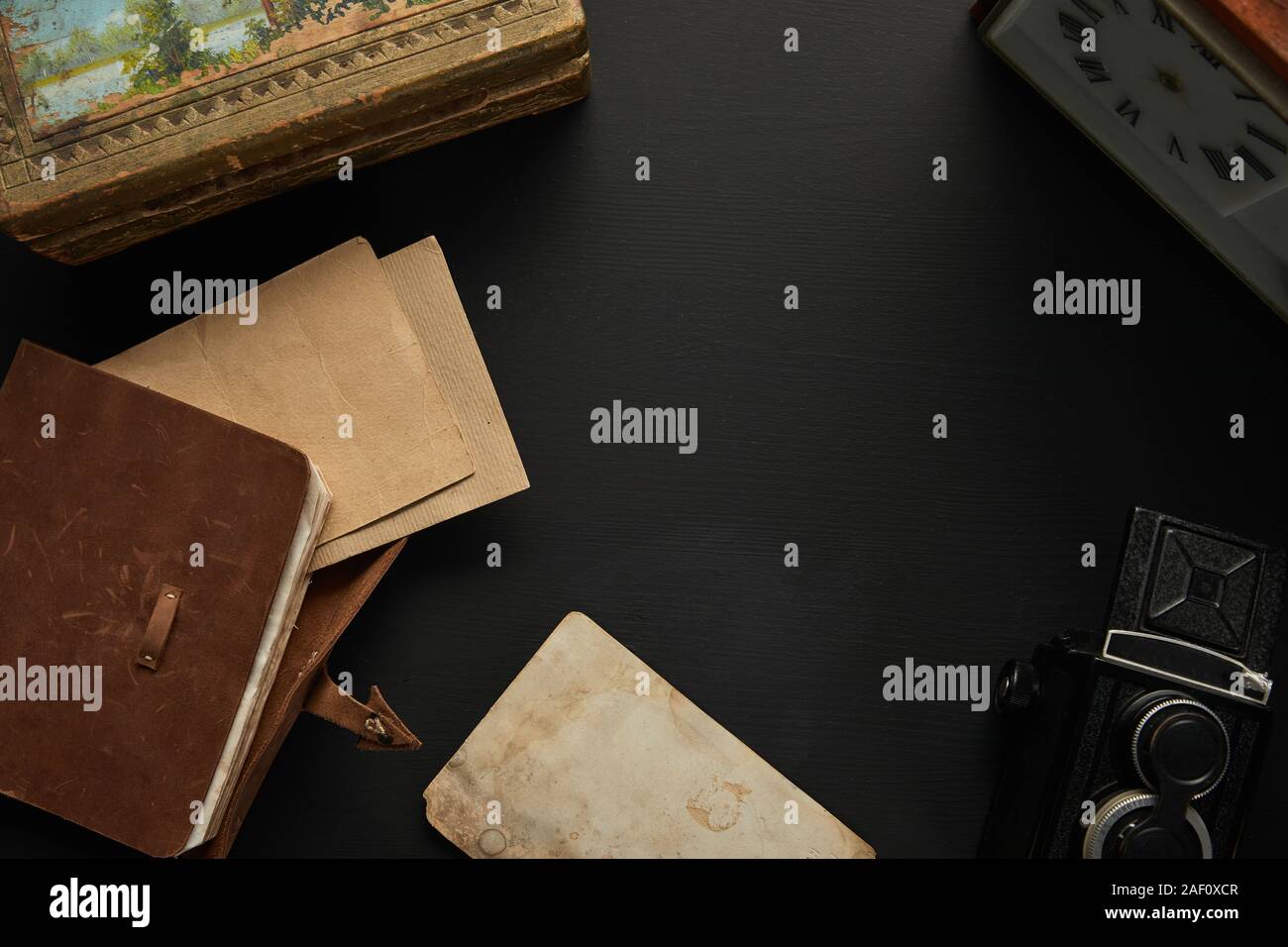 top view of vintage camera, paper, painting, clock and notepad on black ...