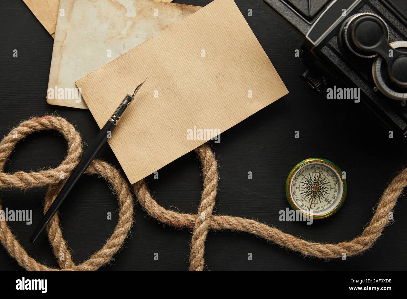top view of vintage camera, paper, rope, fountain pen, compass on black ...