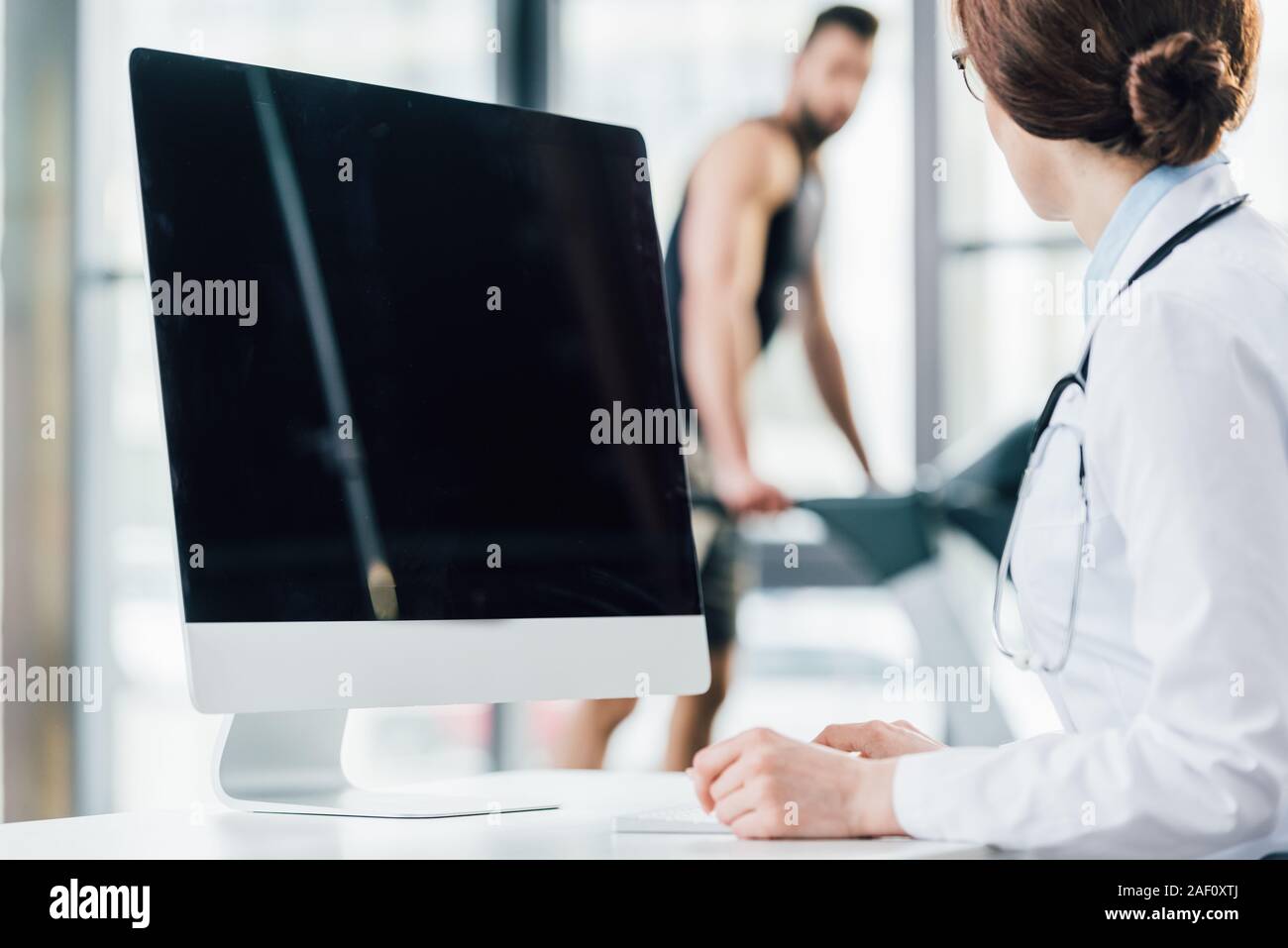 selective focus of doctor sitting near computer with blank screen in ...
