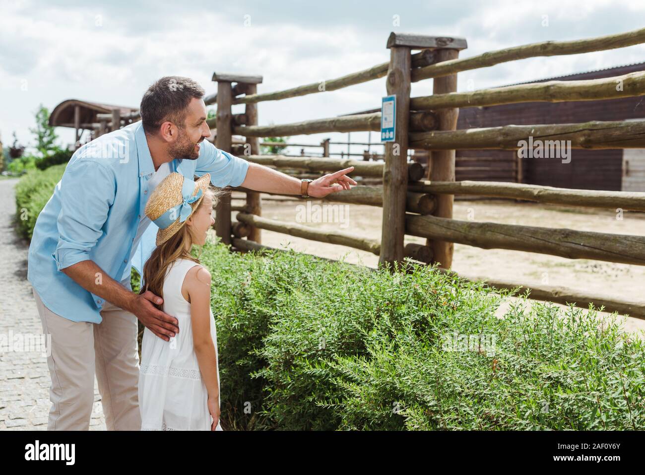 happy man pointing with finger near daughter in straw hat and dress ...