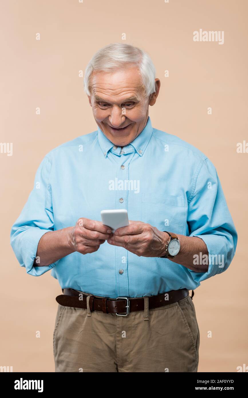 happy retired man with grey hair using smartphone isolated on beige ...