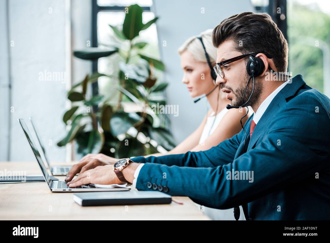 selective focus of handsome man in headset typing on laptop while ...