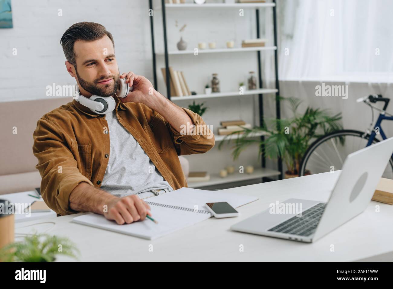 handsome man with headphones looking at screen of laptop and holding ...