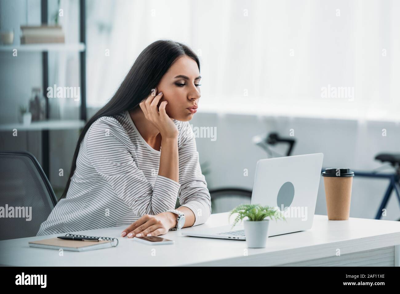 beautiful and brunette woman looking at screen of laptop and making ...