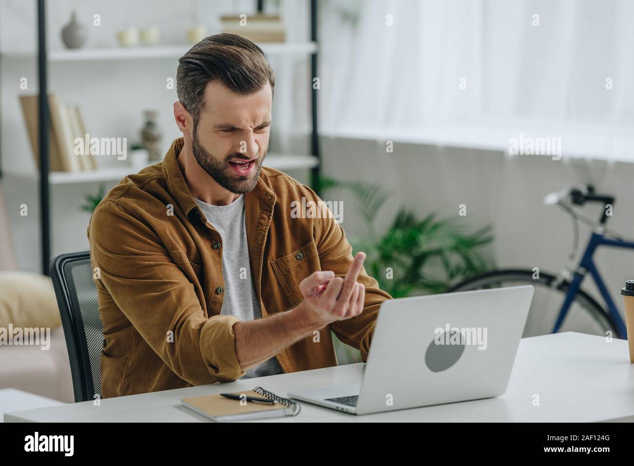 handsome and aggressive man showing middle finger at screen of laptop ...