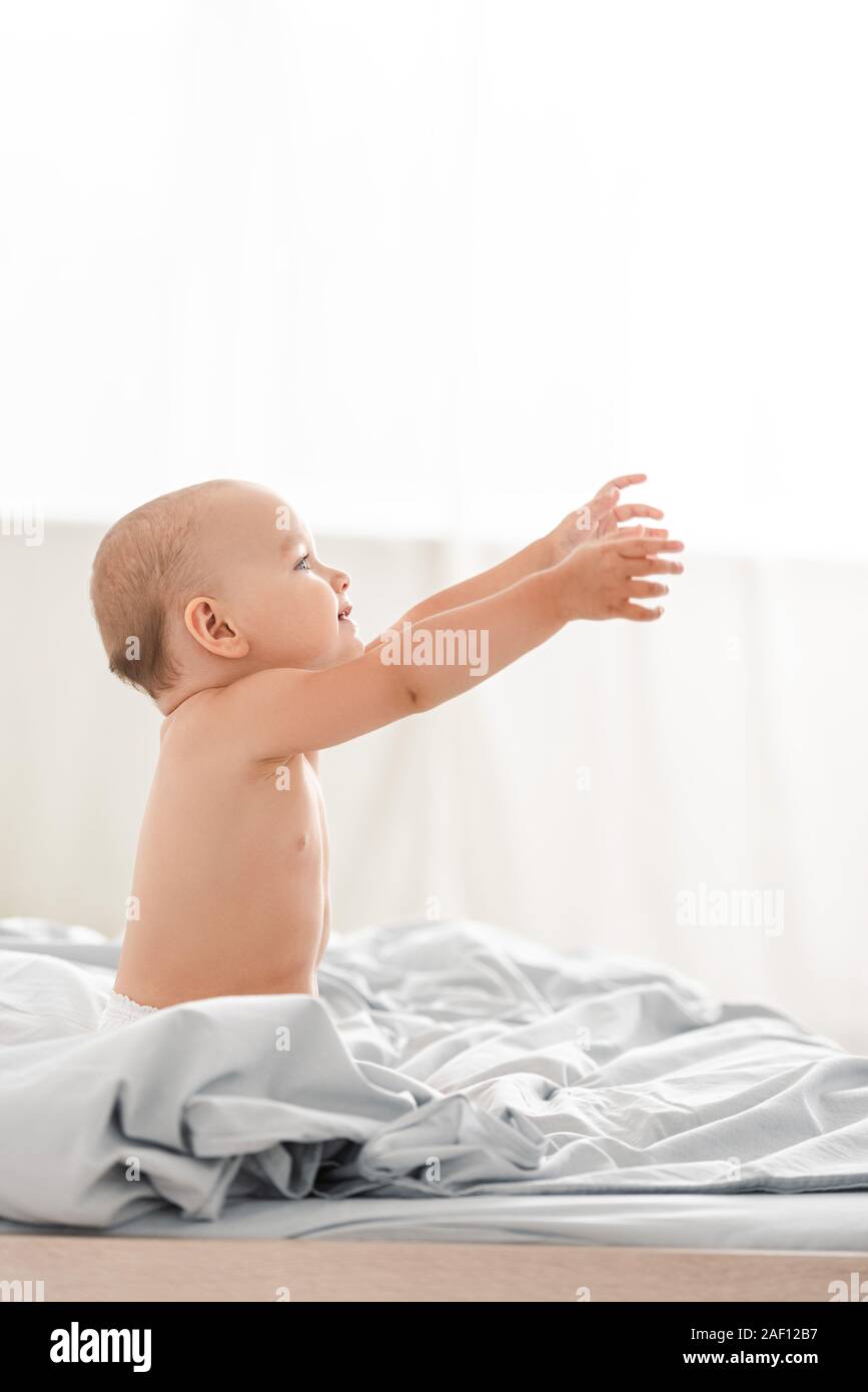 Side view of cute little child in diaper smiling and raising hands up ...